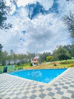 Uma piscina com ladrilhos quadriculados, um edifício com telhado vermelho e uma placa com a inscrição "HOTEL".