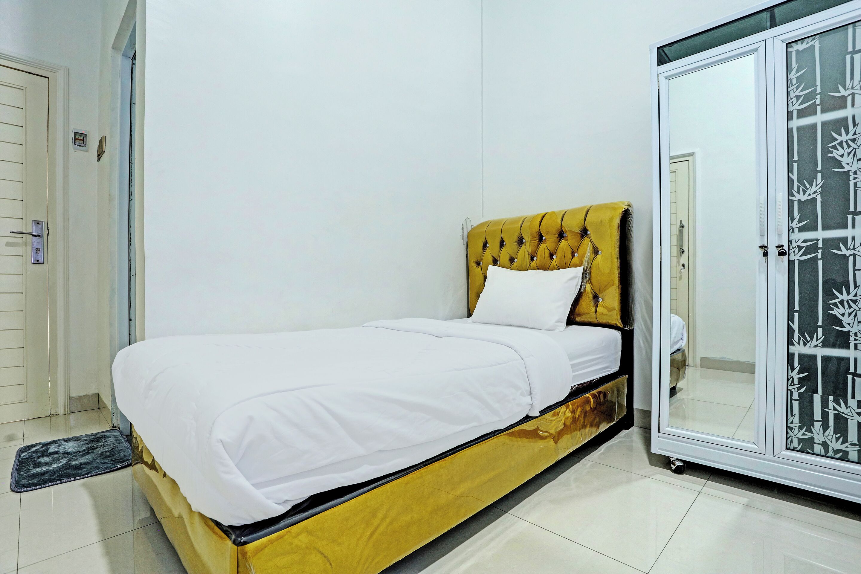 Cama de solteiro com colchão branco e cabeceira amarela em quarto com paredes brancas e um amplo armário espelho com padrão de bambu.