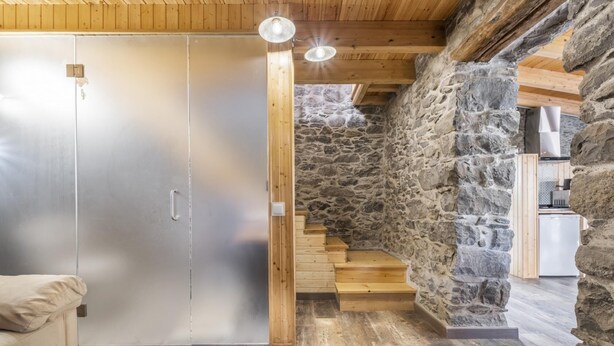 Quarto com parede de pedra, escada de madeira e porta deslizante.