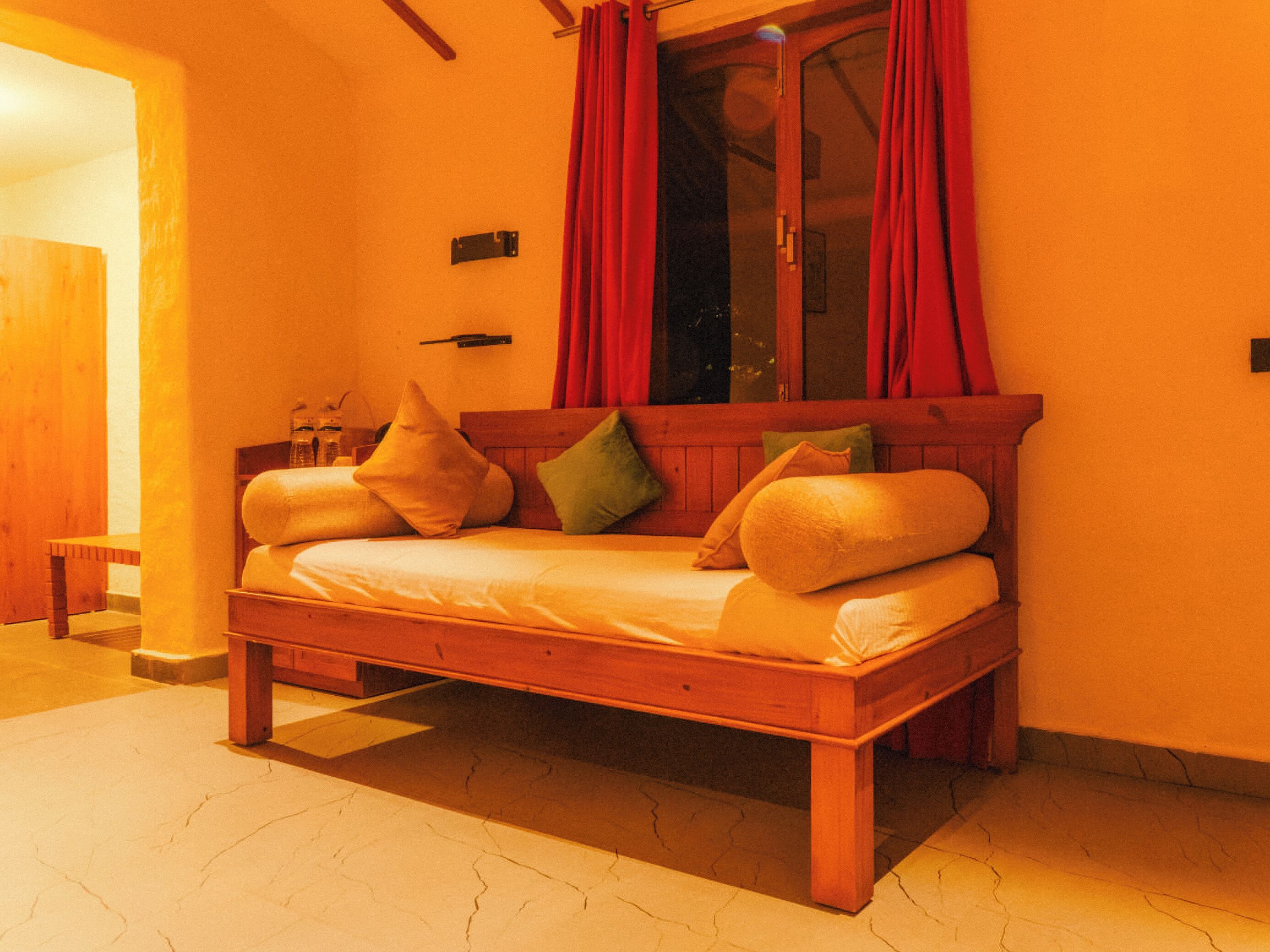 Uma cama de madeira com almofadas, uma janela com cortinas e um chão de madeira.