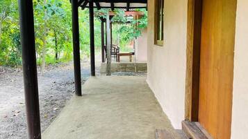 Uma área externa coberta com piso de concreto, degraus de madeira que levam a uma porta e um banco sob uma pérgola.
