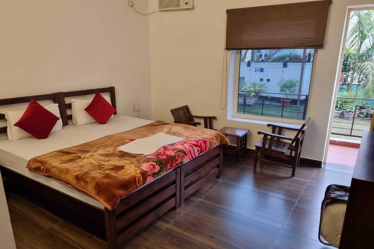 Quarto com cama de madeira, uma secretária pequena e janela com vista para um edifício e áreas verdes.