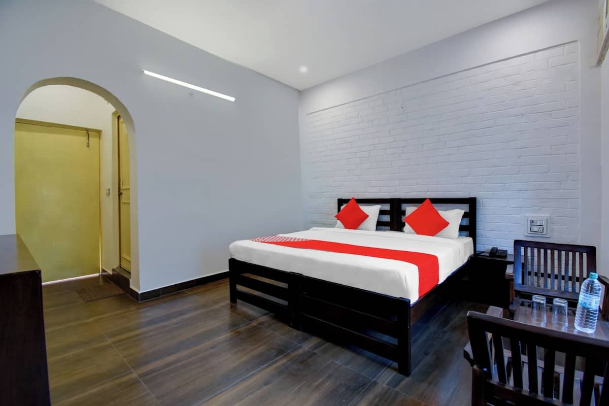 Quarto de hotel com cama, mesa de cabeceira, cadeira de madeira e mesa com garrafa e copos.