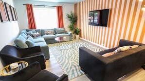 Uma sala de estar moderna com um sofá modular, uma mesa de centro redonda e uma TV de tela plana na parede.