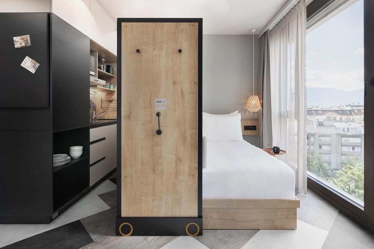 Quarto de hotel moderno com uma cama grande, um guarda-roupa, uma escrivaninha e vista para a cidade.