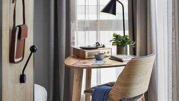 Um quarto com uma mesa de madeira, uma cadeira, um abajur, uma planta e uma janela com cortinas.
