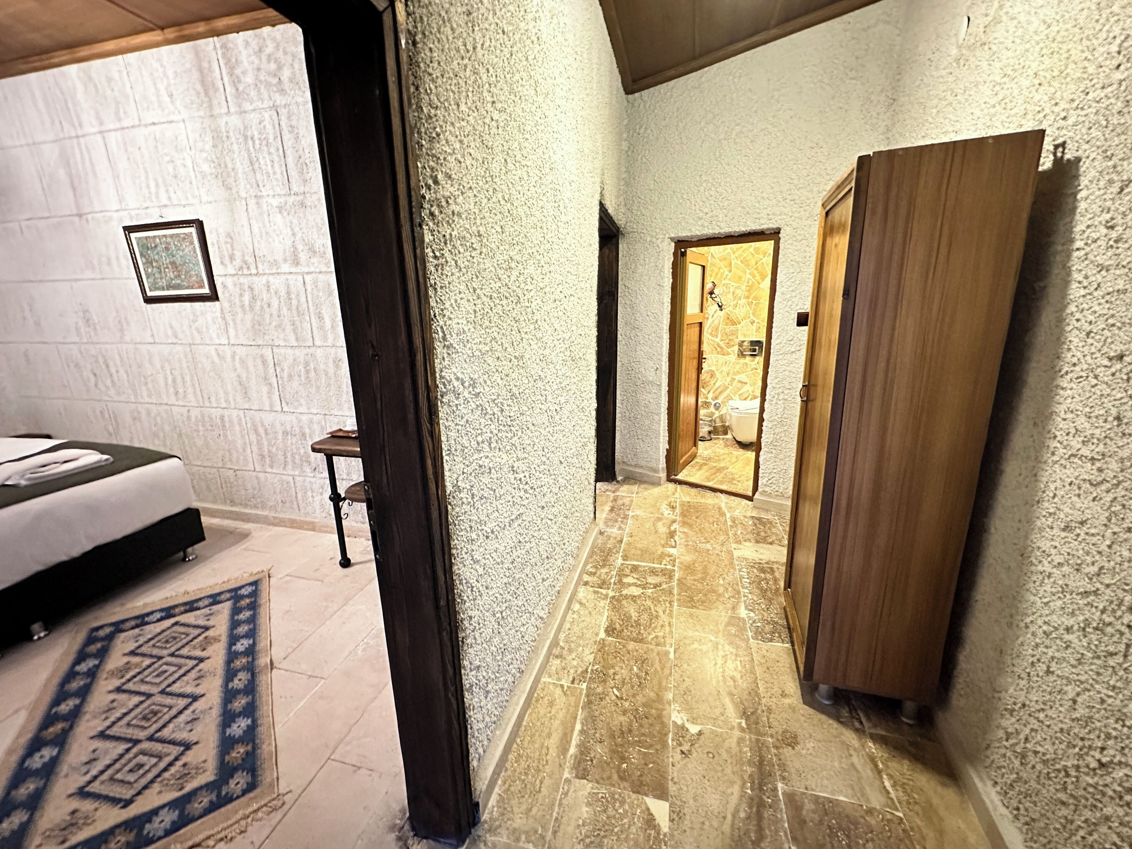 Um corredor com uma cama, uma mesa pequena e uma porta que dá para um banheiro.