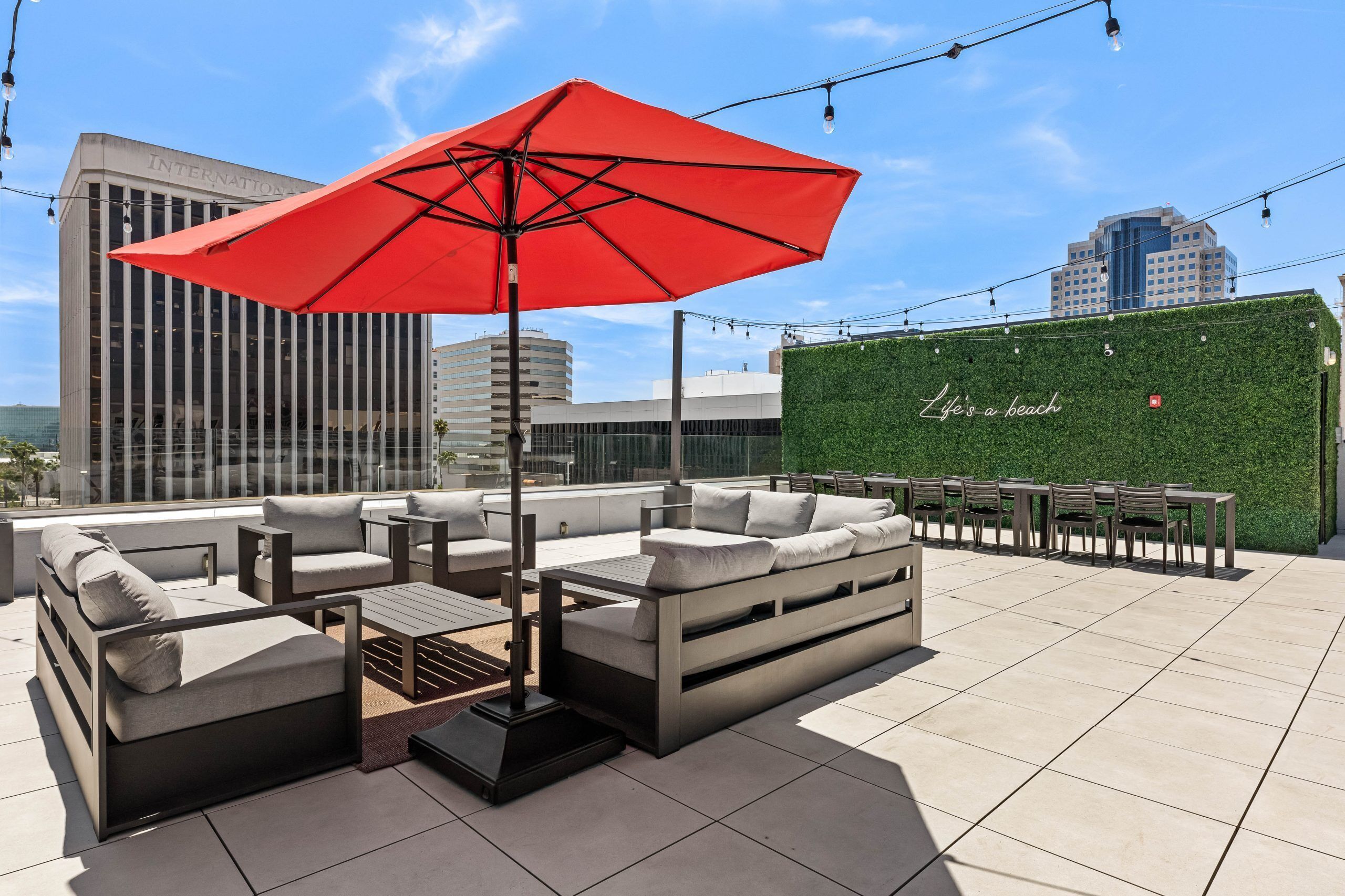 Terraço no telhado com área de estar ao ar livre, um guarda-sol vermelho e vista para a paisagem urbana.