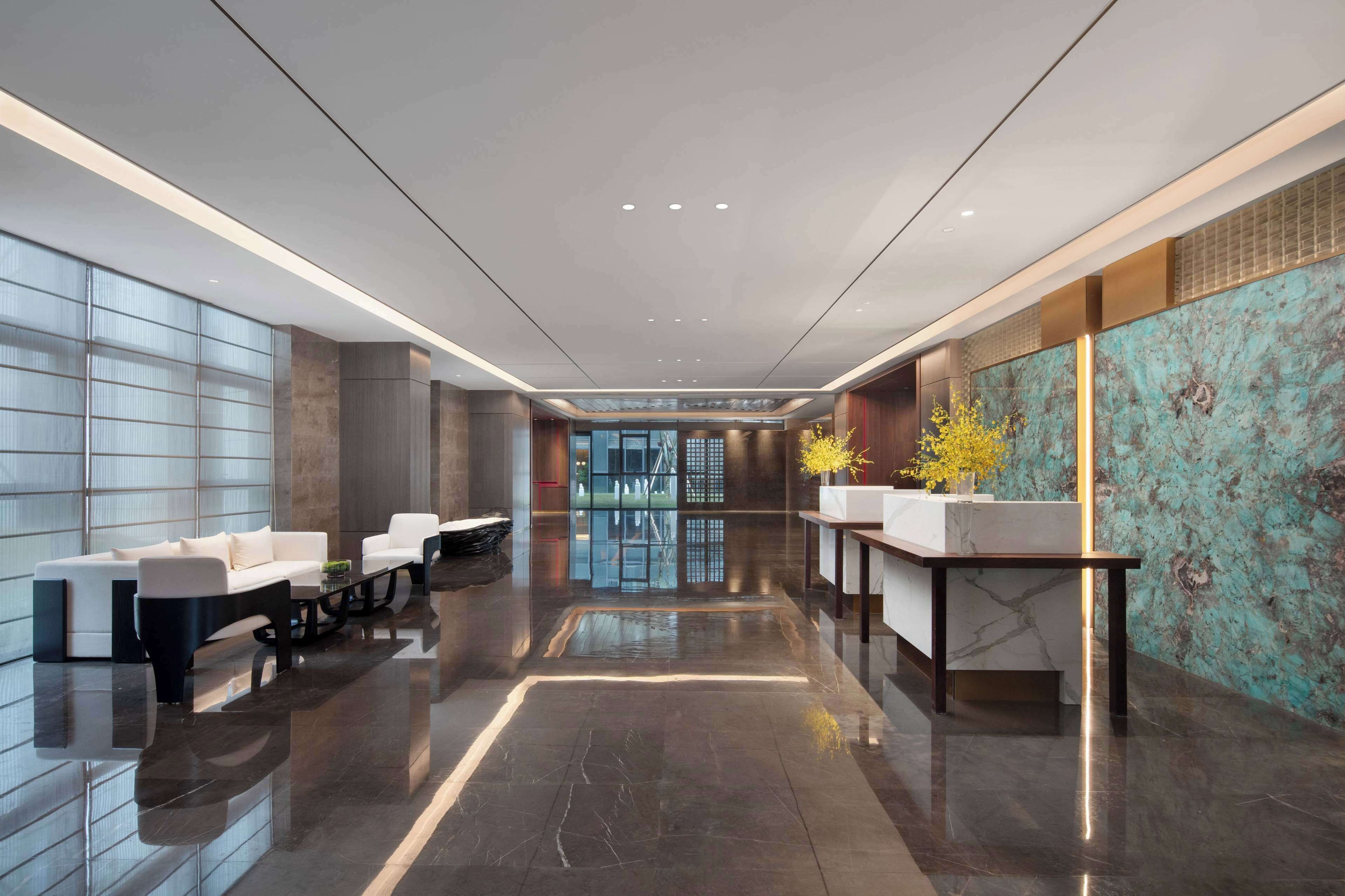 Um lobby moderno com um balcão de recepção extenso, área de estar e uma porta de vidro para o exterior.