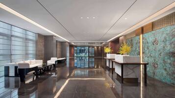 Um lobby moderno com um balcão de recepção extenso, área de estar e uma porta de vidro para o exterior.