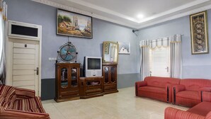 Uma sala de estar com televisão, armário de madeira e sofá vermelho.