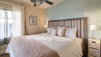 Quarto com cama grande, ventoinha no teto, janela com cortinas e mesa de cabeceira com abajur.