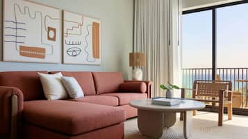 Uma sala de estar moderna com um sofá, uma mesa de centro redonda e vista para o mar através de uma varanda.
