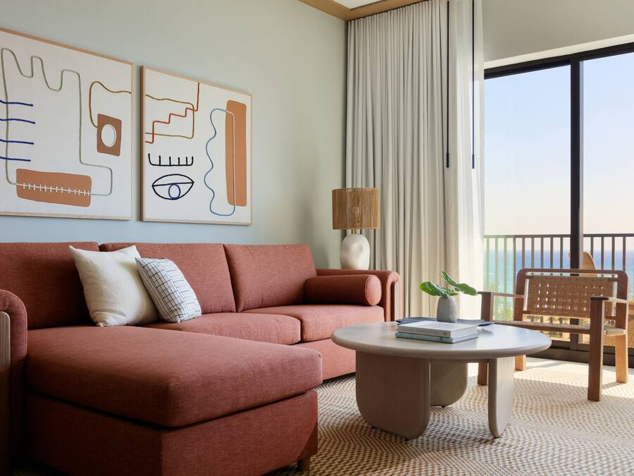 Uma sala de estar moderna com um sofá, uma mesa de centro redonda e vista para o mar através de uma varanda.