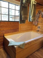 Quarto de cabana de madeira com uma banheira grande, paredes de madeira e uma janela com persianas.