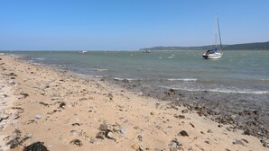 Uma praia com um veleiro, costa rochosa e mar calmo.