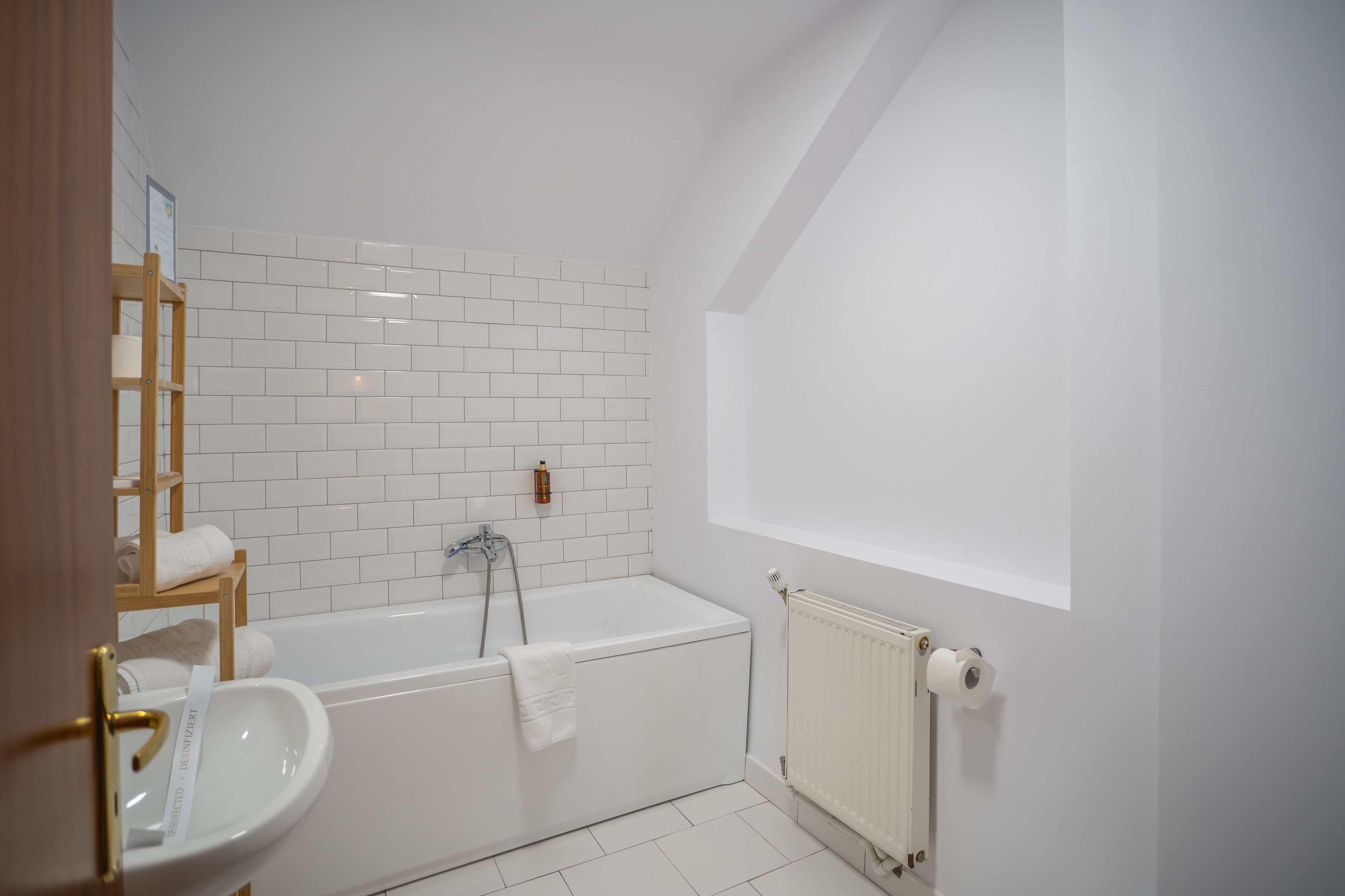 Casa de banho moderna com uma banheira branca, uma prateleira de madeira com toalhas, uma pia branca e um radiador branco.