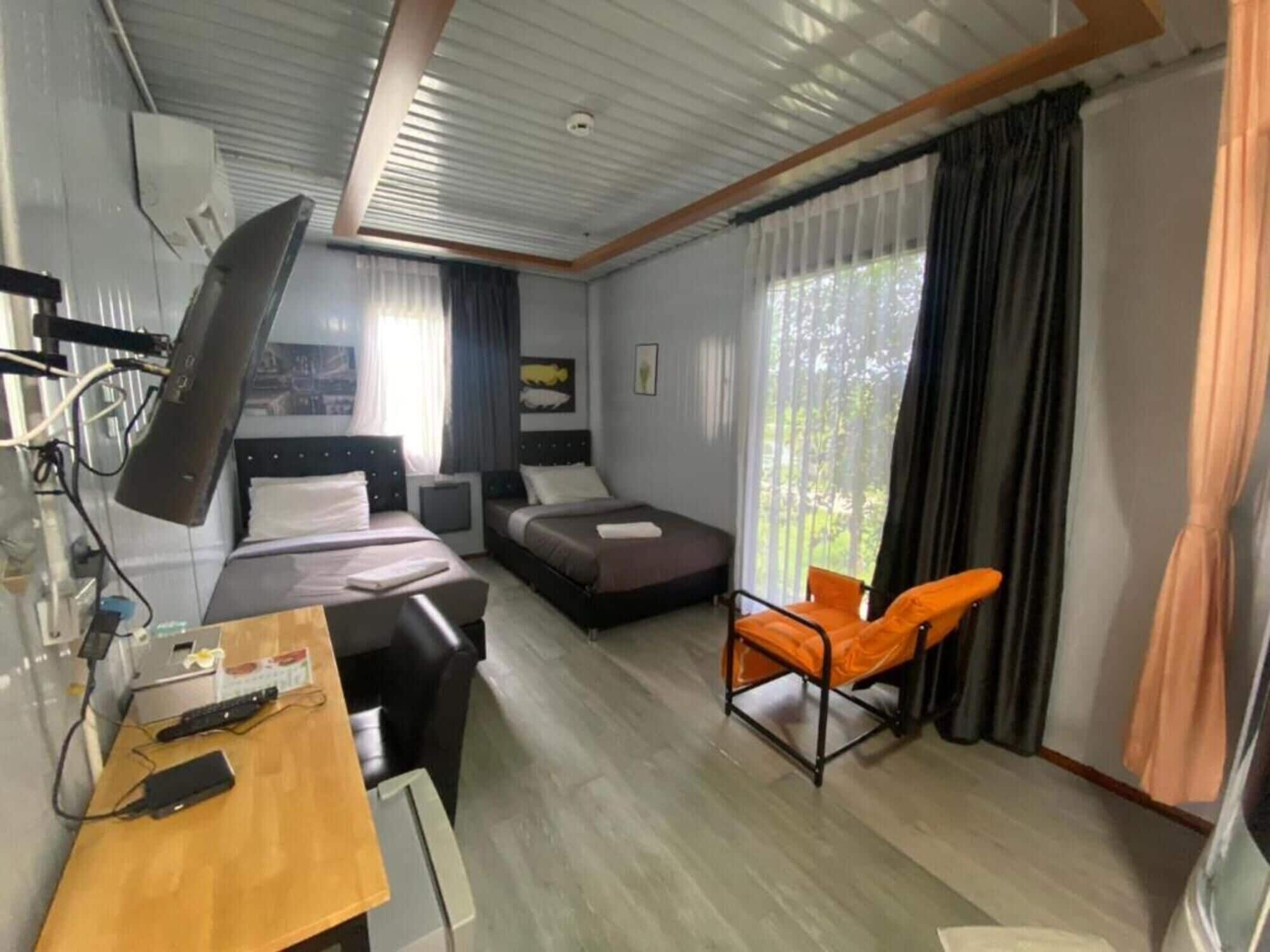 Quarto de hotel com cama, escrivaninha, cadeira, televisão e janela com cortinas.
