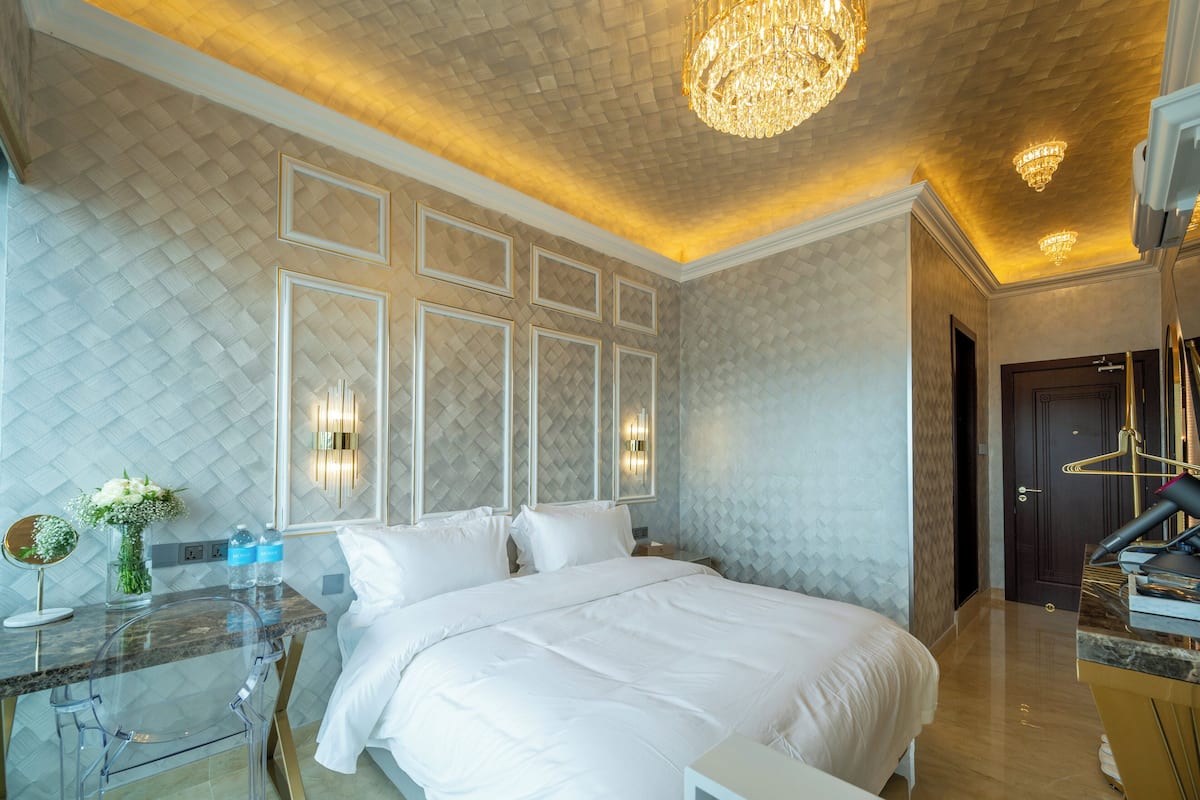 Um quarto espaçoso com uma cama grande, uma mesa de vidro com um vaso de flores e um candelabro.