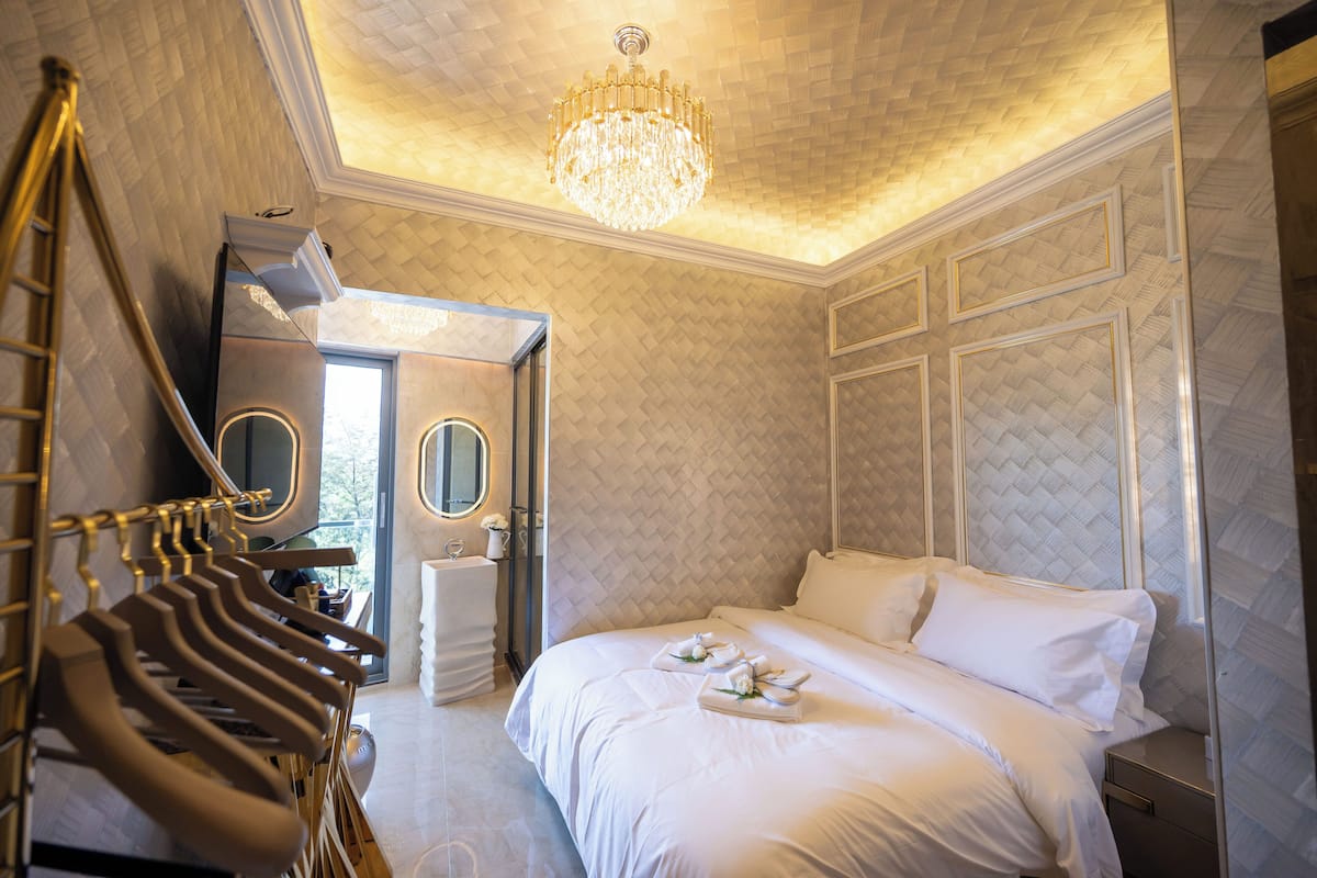 Quarto de hotel com cama, lustre, guarda-roupa e espelho.