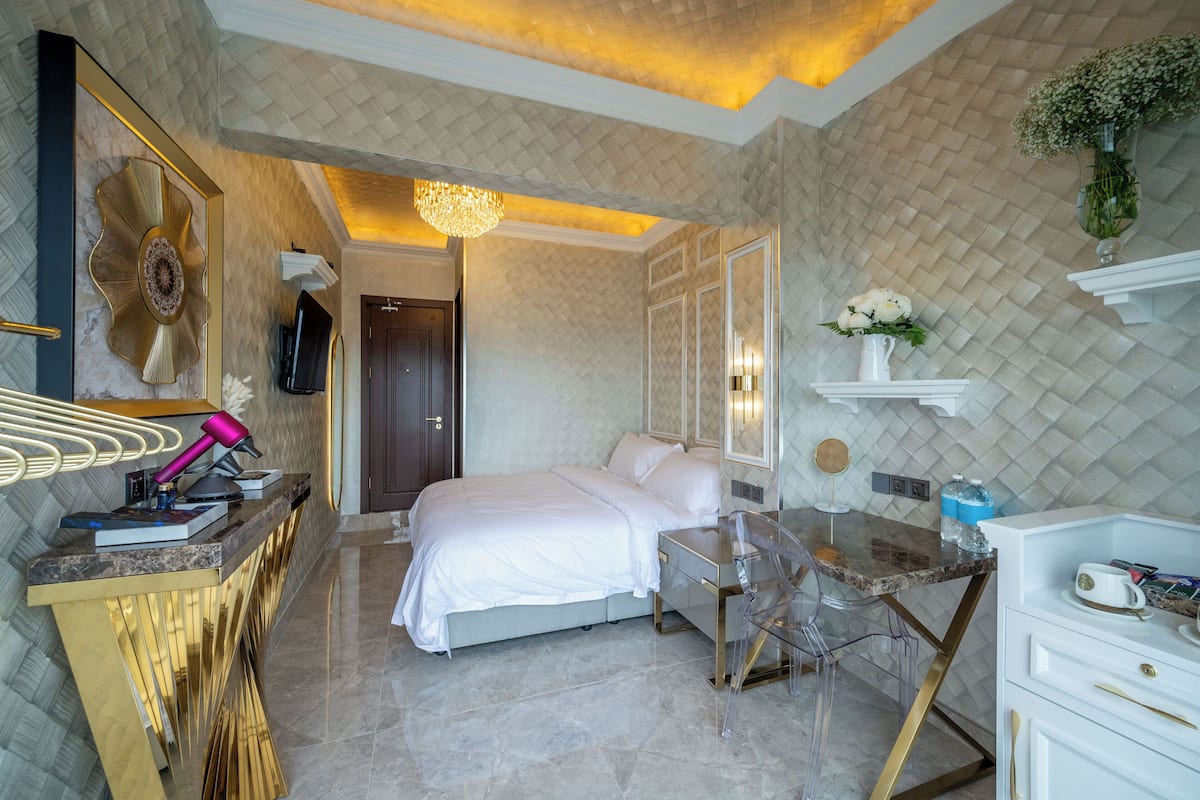 Quarto de hotel moderno com uma cama, uma escrivaninha com cadeira, uma toucador com espelho e um candelabro.
