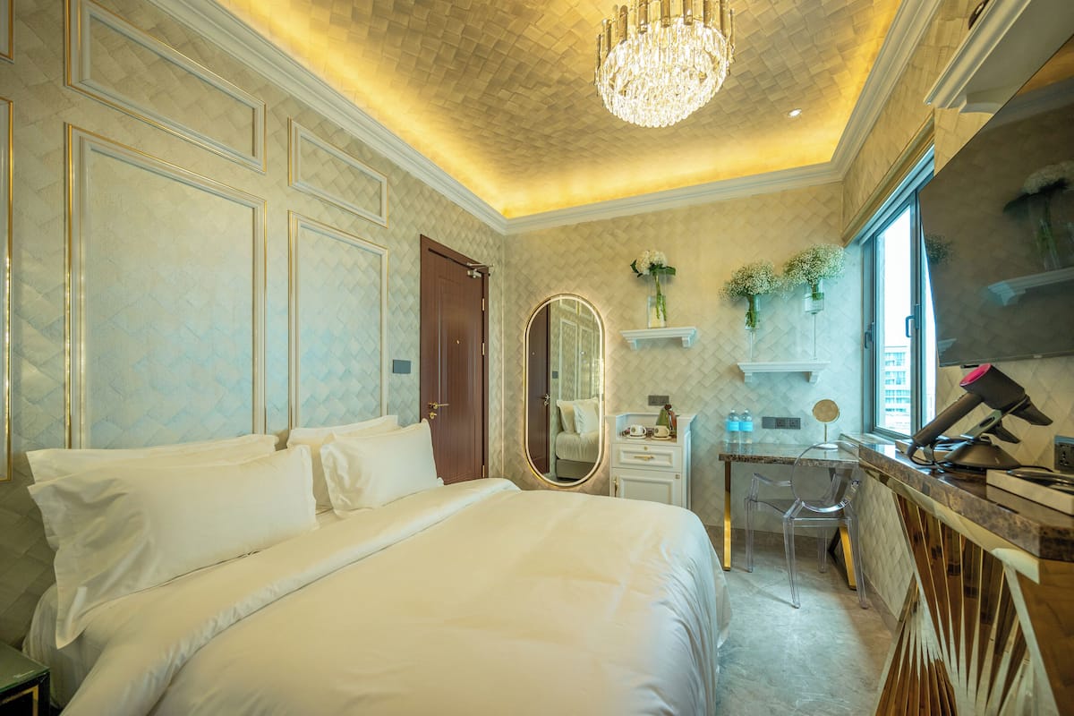 Quarto de hotel com uma cama grande, uma escrivaninha, uma cadeira, um espelho e um candelabro.