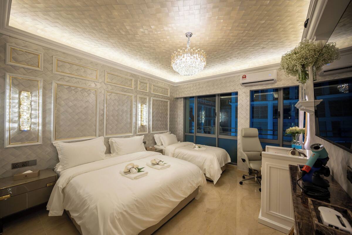 Quarto de hotel com duas camas, uma escrivaninha com computador e uma janela grande com vista para a cidade.
