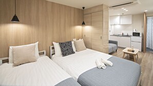 Quarto de hotel com duas camas, uma cozinha compacta e um pequeno espaço de estar.