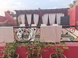Uma varanda com plantas em vasos, cortinas brancas e guarda-corrimão de metal.