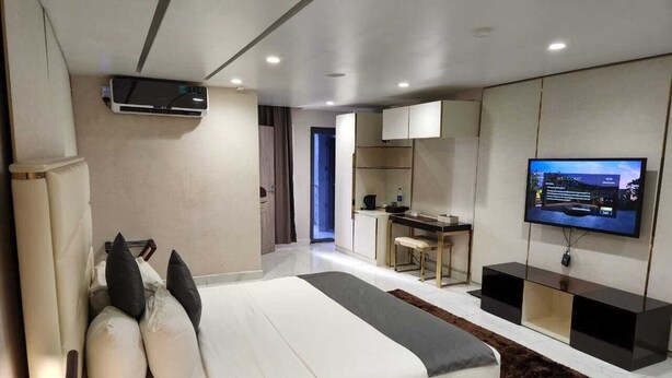 Quarto moderno com cama grande, televisão e pequena cozinha.