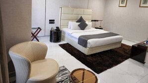 Quarto de hotel moderno com uma cama grande, uma mesa de cabeceira, uma cadeira e uma mesinha.