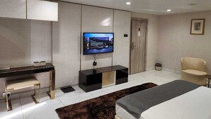 Quarto de hotel moderno com televisão de tela plana na parede, uma escrivaninha com cadeira, cama com cabeceira e um sofá.