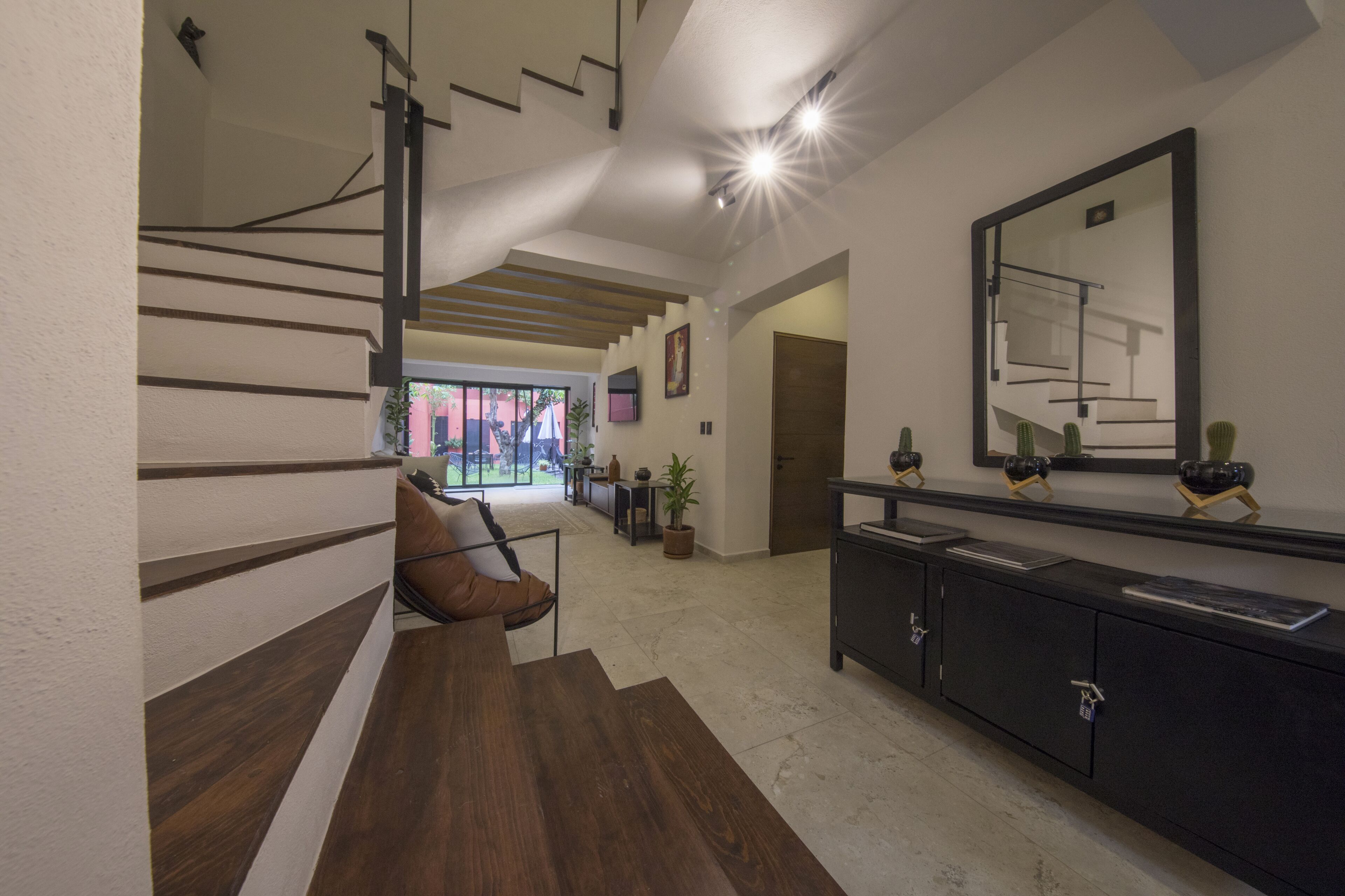 Um interior moderno com escada, sofá, mesa de jantar, armário preto e um espelho grande.