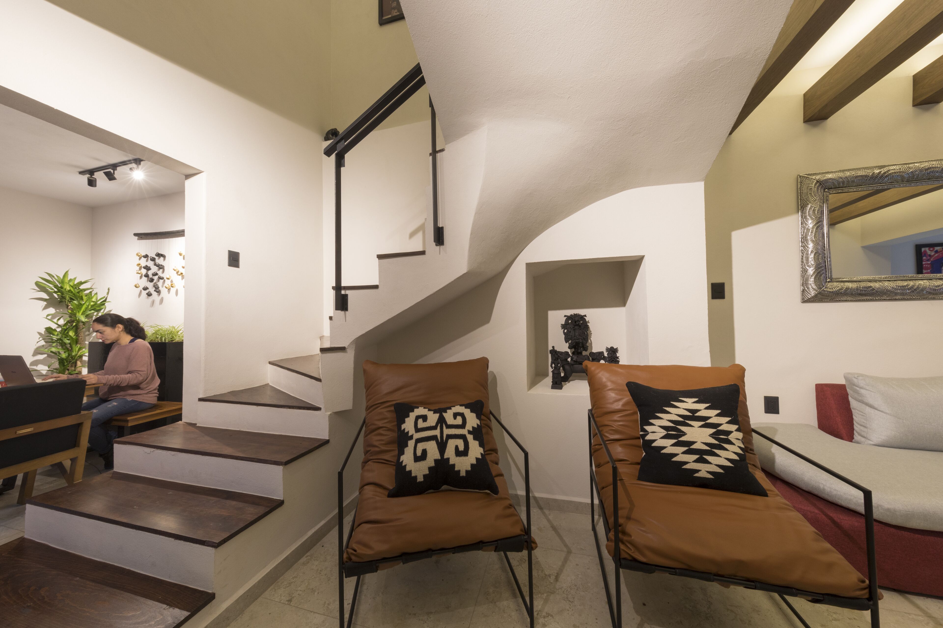 Um interior moderno com escada, sofá e poltrona com almofadas estampadas.