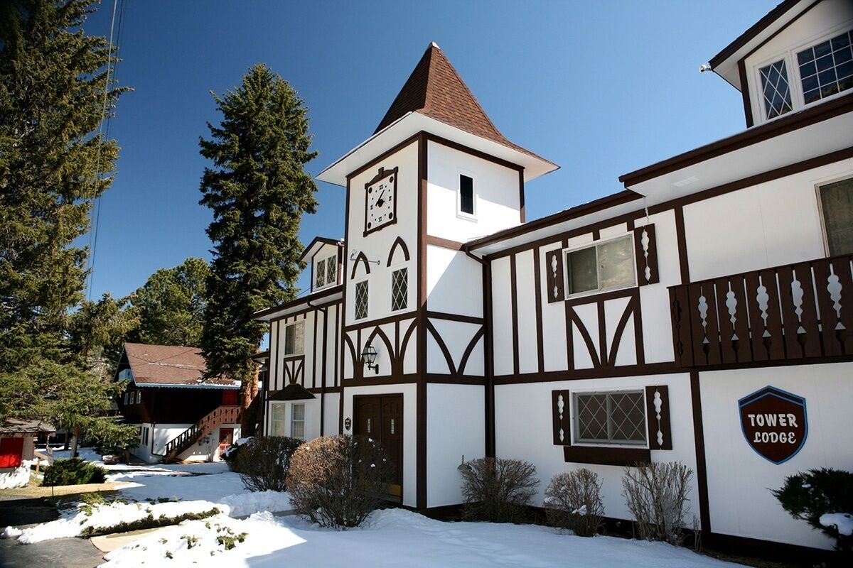 Um edifício em estilo Tudor tradicional, com uma torre e relógio destacados, rodeado por terreno e árvores cobertos de neve.