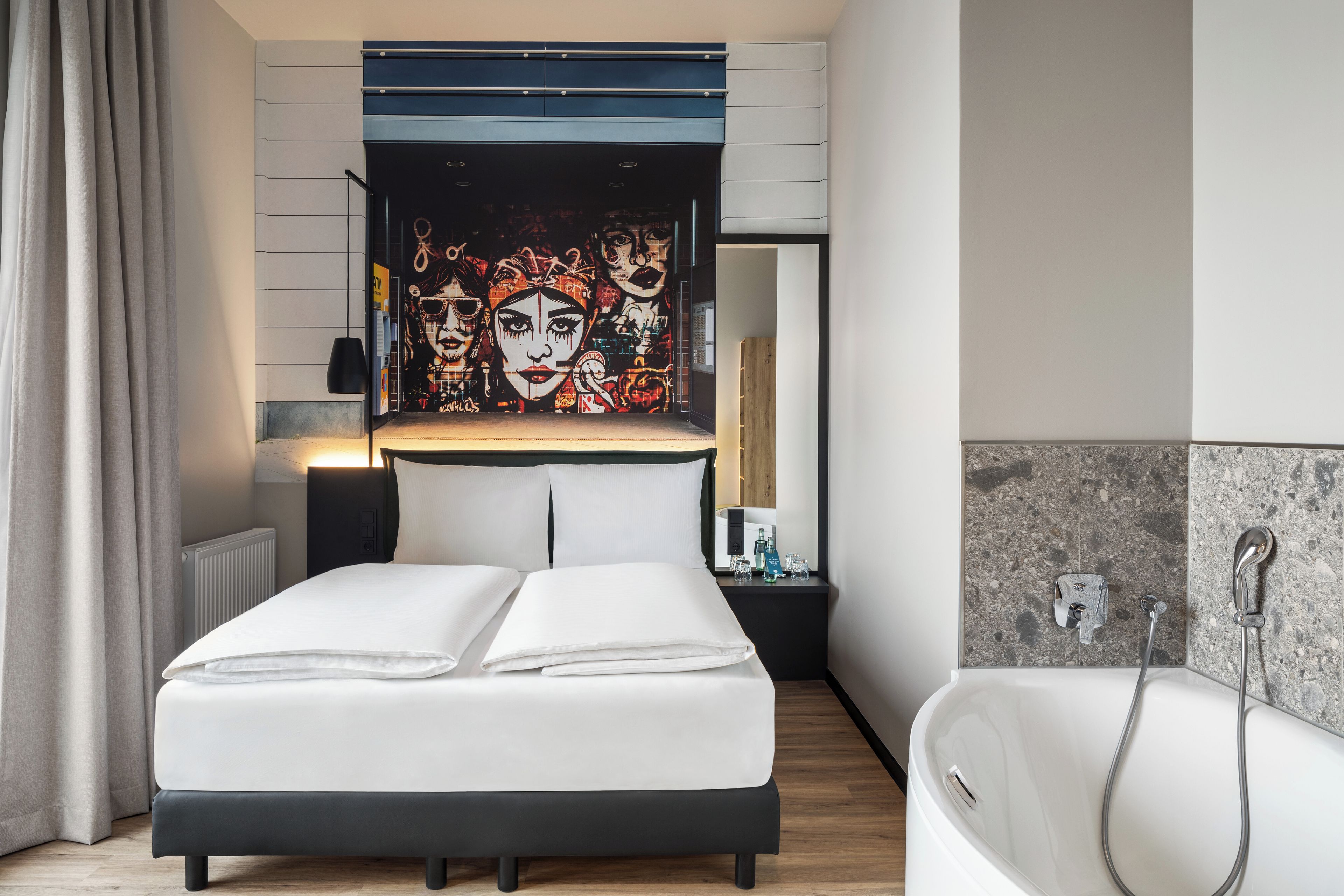 Quarto moderno com uma cama grande, banheiro com banheira e um mural na parede.