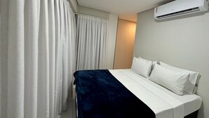 Quarto de hotel com uma cama, cortinas brancas e um aparelho de ar condicionado na parede.