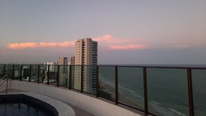 Piscina no terraço com vista para o oceano e para a cidade ao pôr do sol.