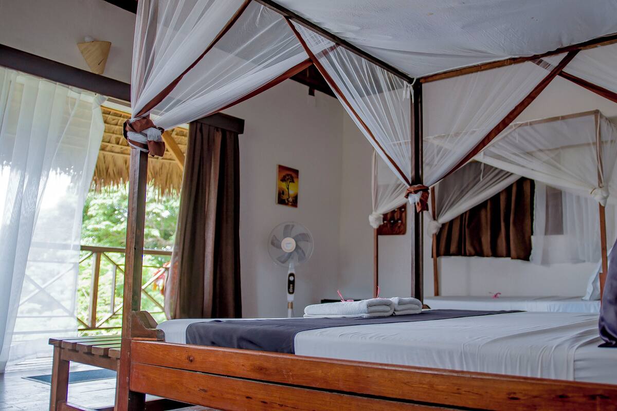 Quarto com cama, ventoinha e vista para o verde lá fora.