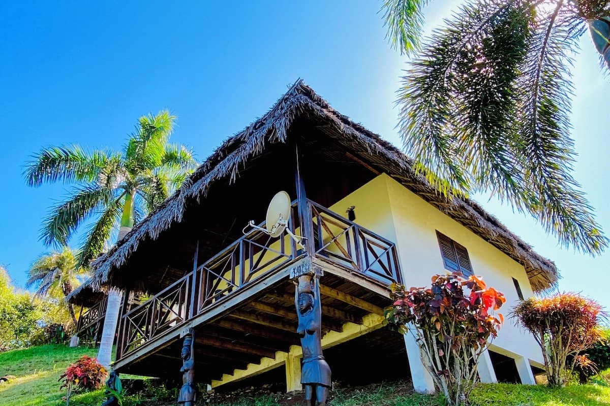 Uma casa com telhado de colmo, varanda e escadaria que leva à entrada.