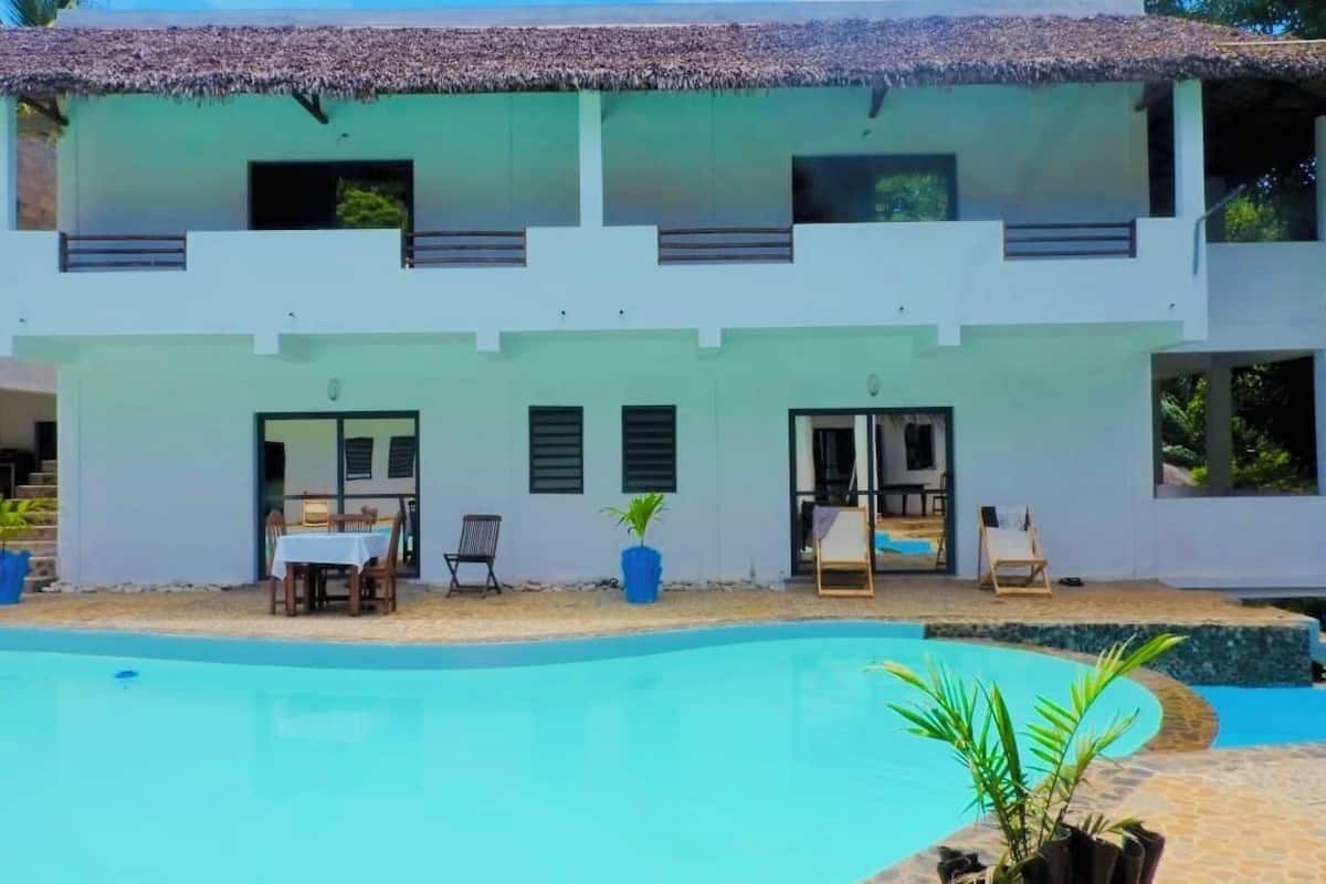 Um edifício de dois andares com piscina, área de estar externa e telhado de palha.