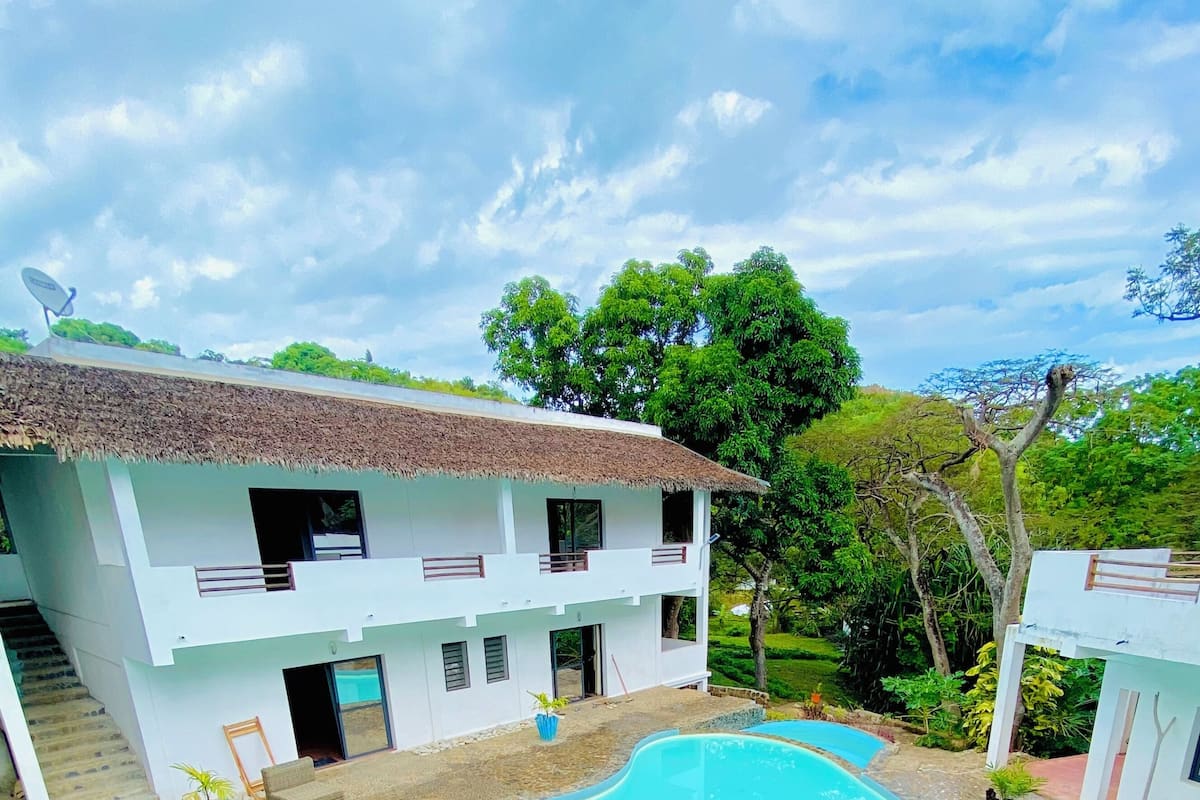 Uma piscina com borda curva, um edifício branco com várias varandas e uma antena parabólica.