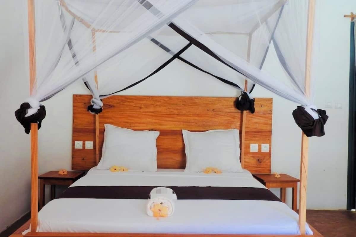 Uma cama com cabeceira de madeira, roupa de cama branca e mosquiteiro.