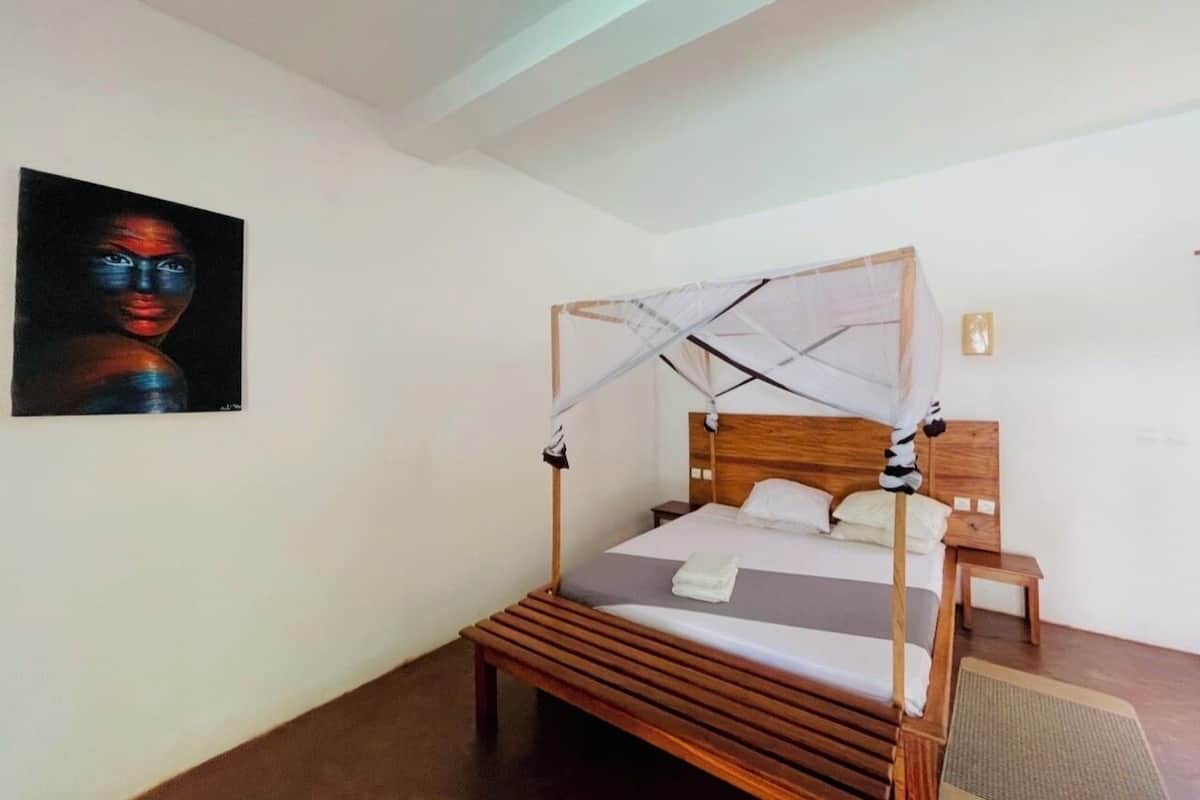 Quarto com cama de madeira, mesa de cabeceira, luminária e um ventilador no teto.