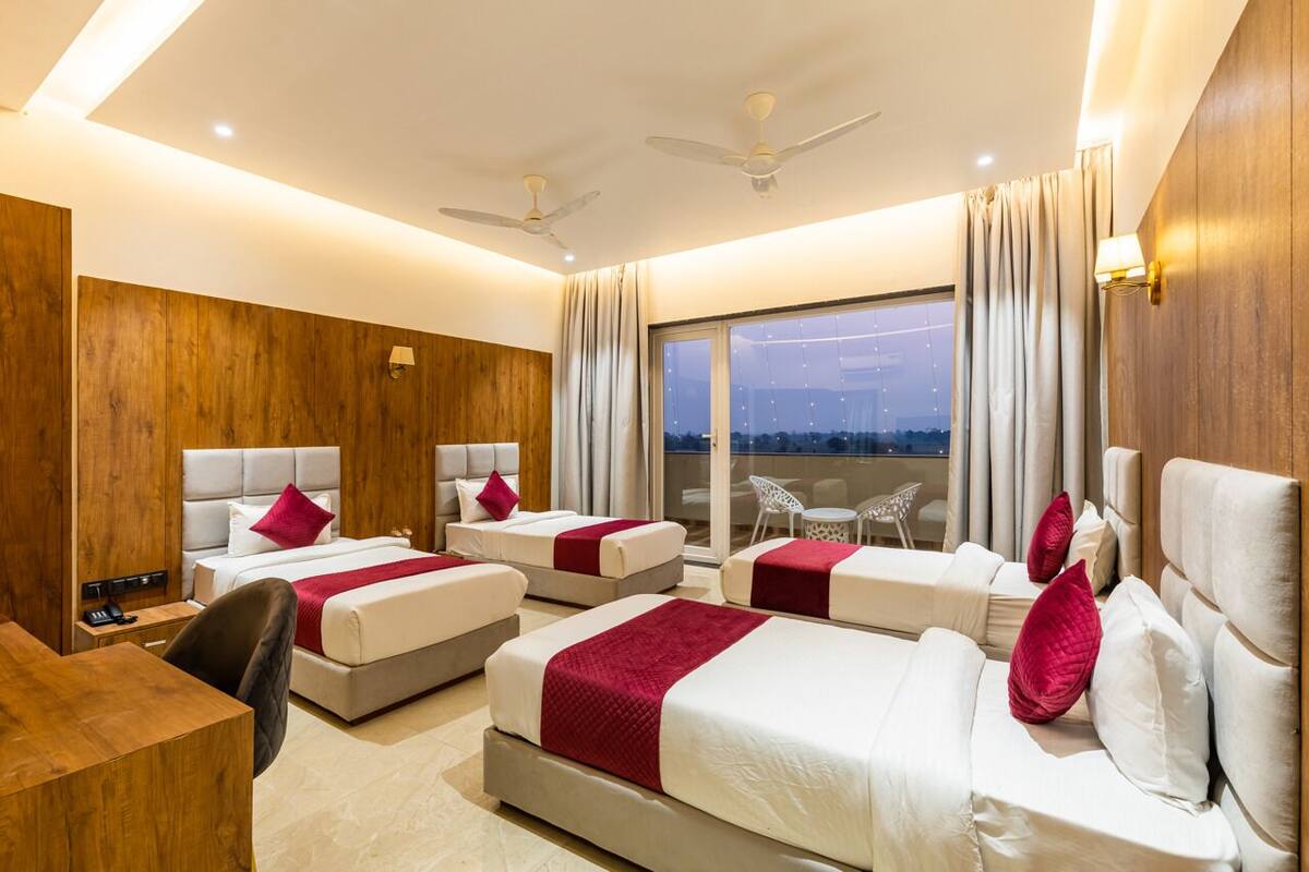 Quarto de hotel com quatro camas, uma escrivaninha, uma cadeira e varanda com vista.
