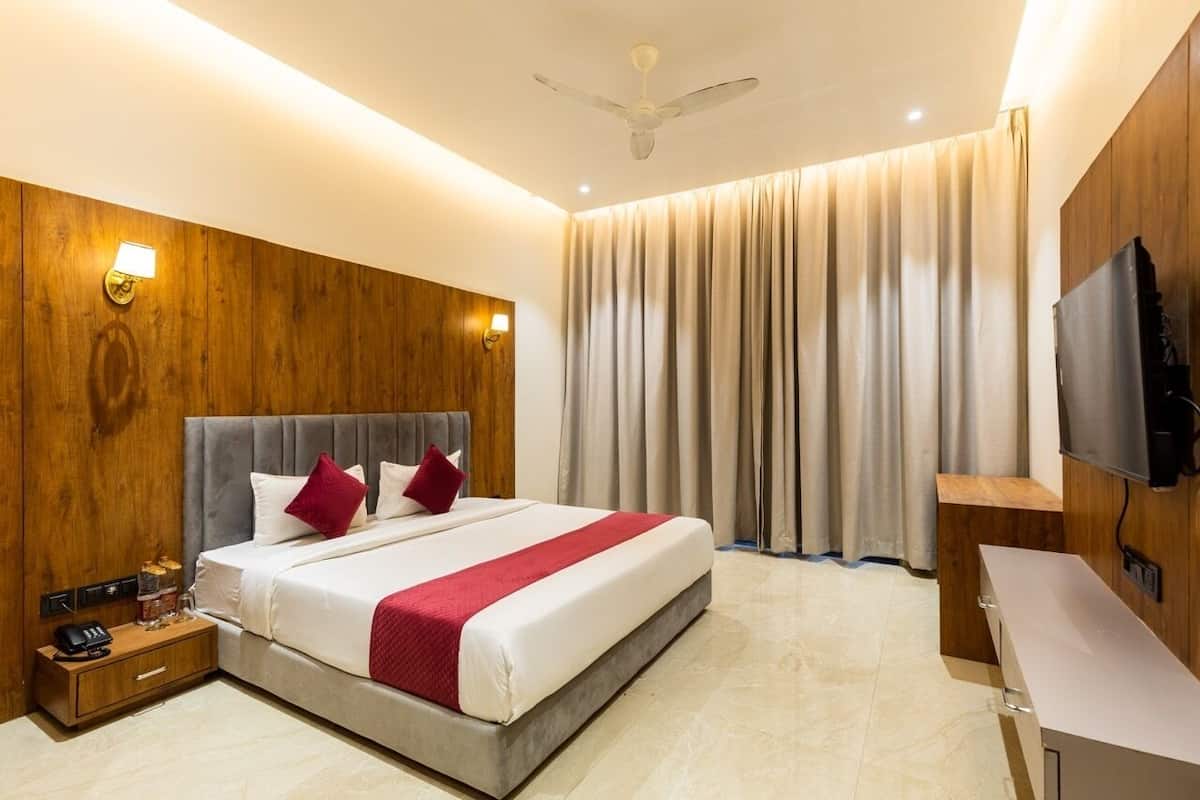 Quarto de hotel moderno com uma cama grande, painéis de madeira, ventoinha no teto e televisão fixada na parede.