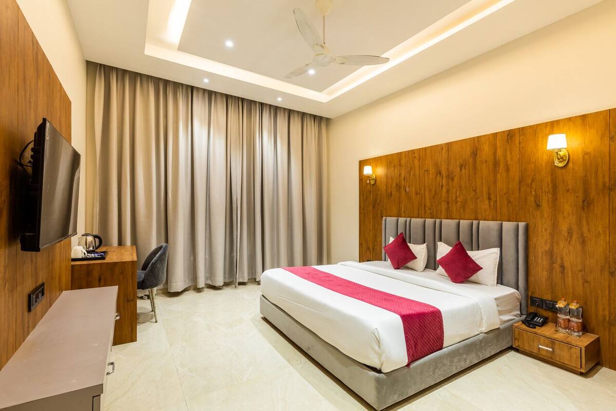 Quarto de hotel moderno com uma cama grande, uma escrivaninha, uma cadeira, uma televisão e um ventilador de teto.