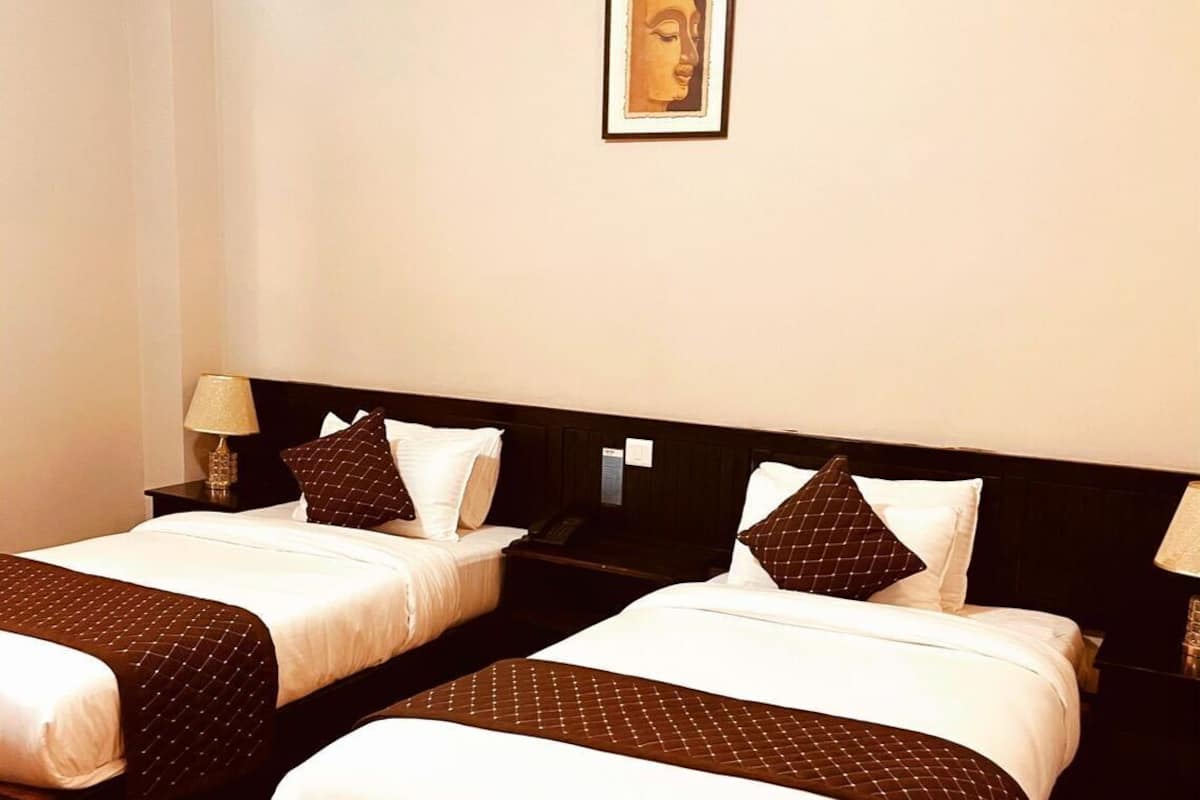 Quarto de hotel com duas camas, piso de madeira e uma moldura com quadro na parede.