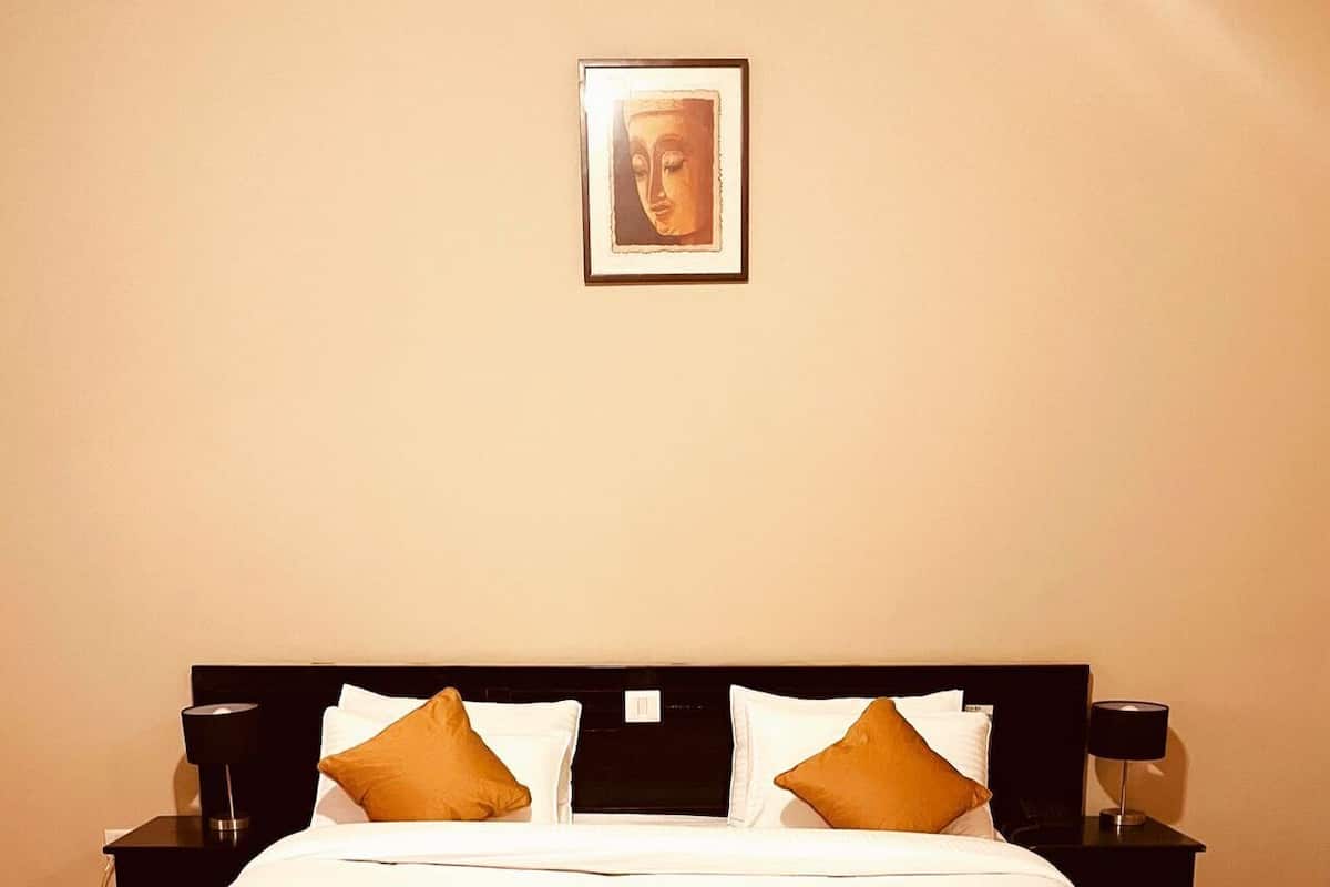 Quarto de hotel com uma cama grande, duas mesas de cabeceira, um quadro na parede e um cobertor marrom.
