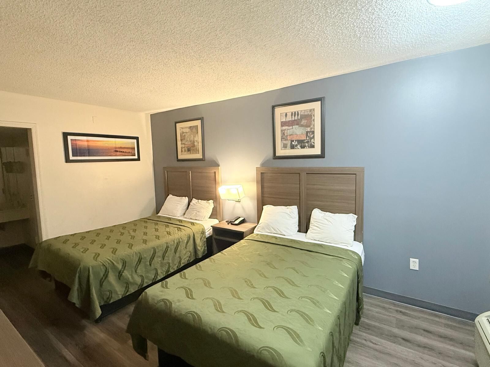 Quarto de hotel com duas camas, mesa de cabeceira com abajur e obras de arte emolduradas nas paredes.